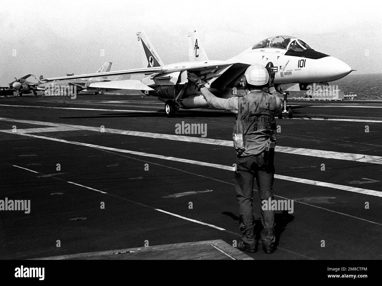 A flight deck crew member signals to the pilot of a Fighter Squadron 14 ...