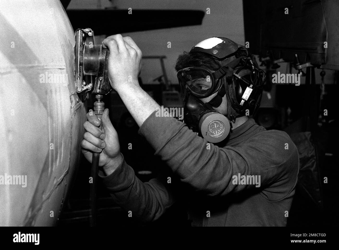 A maintenance crew member wearing protective breathing apparatus sands ...