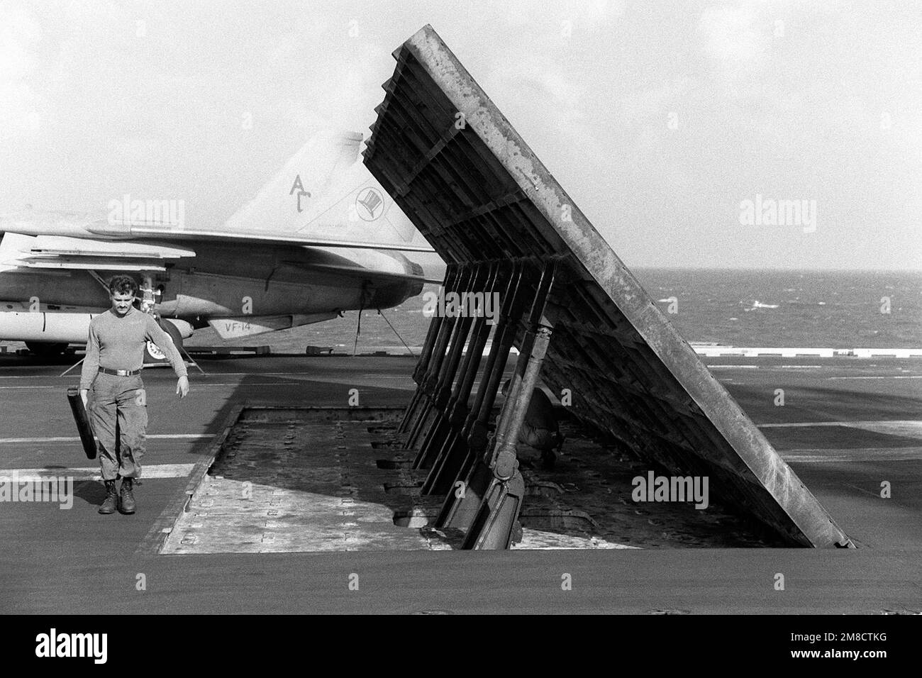 Crewmen check a jet blast deflector near the tail of an aircraft on the ...