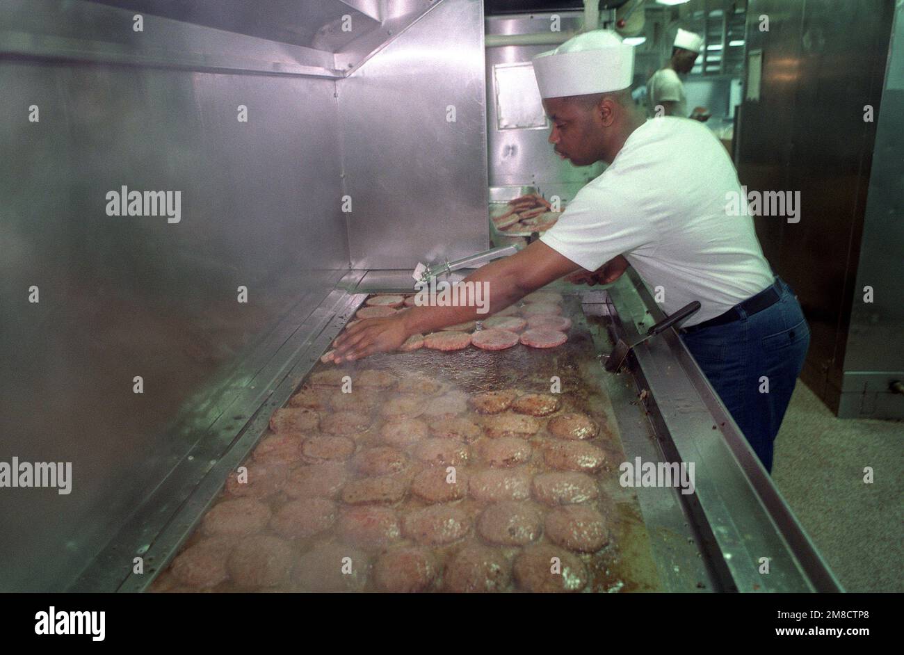 A mess management specialist cooks hamburger patties in the galley of ...