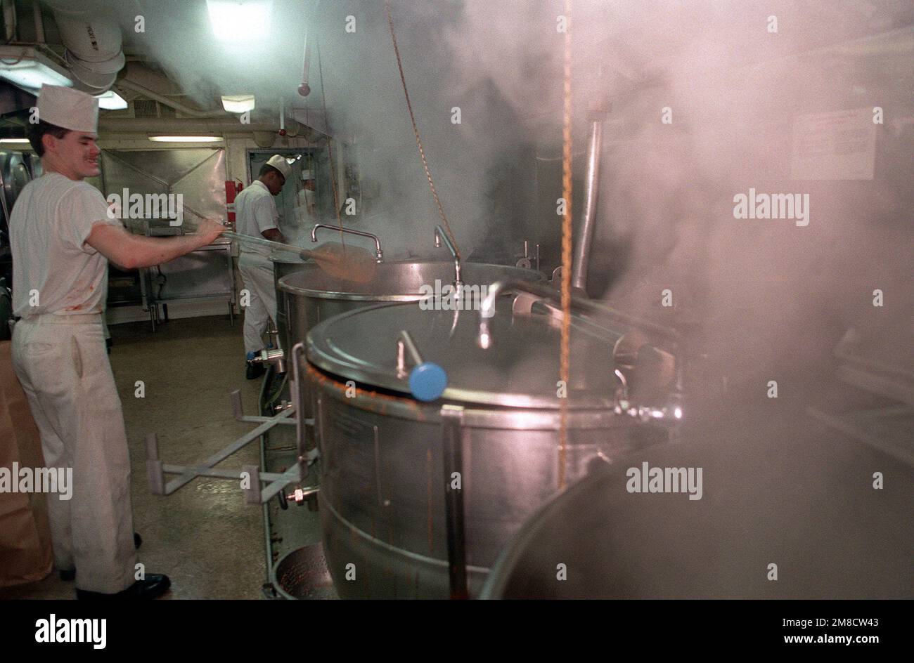 A mess management specialist stirs a kettle of food in the galley of ...