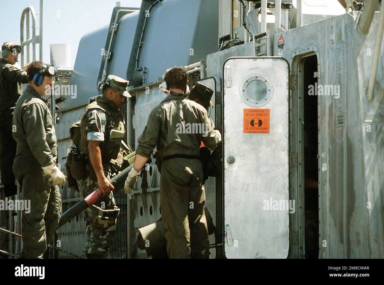 A crewman holds the hatch for two Marines as they enter a compartment ...