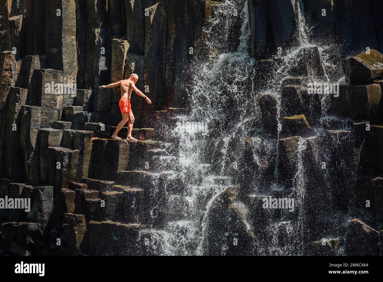 Caucasian man in swimsuit balancing near the falling water streams ...