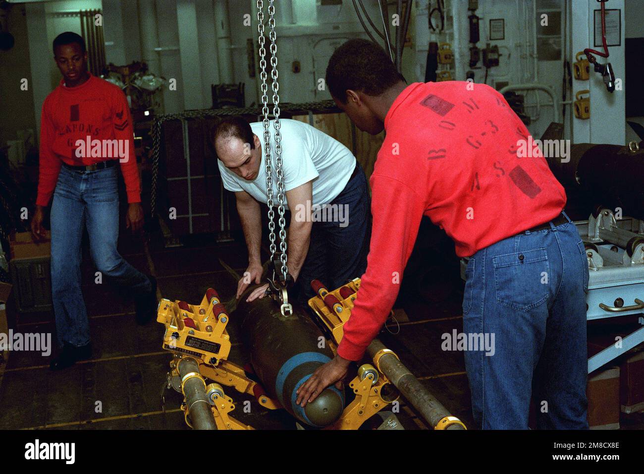 Weapons technicians lower a BDU-45/B 500-pound practice bomb onto an ...
