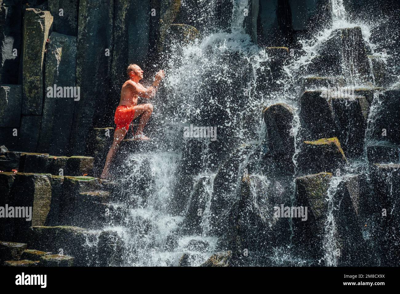 Caucasian man in swimsuit washing his face under the falling water ...
