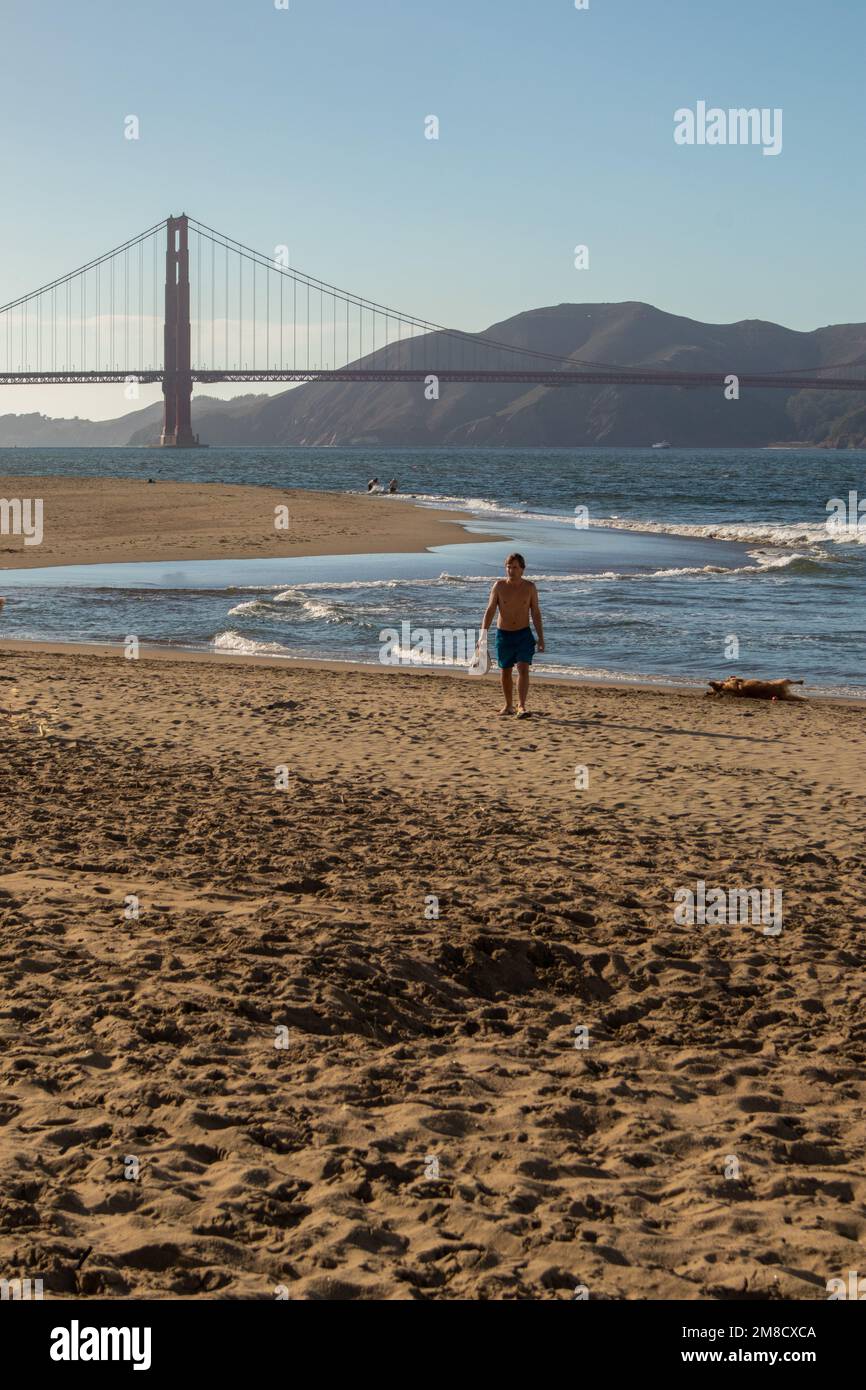 A vertical shot of a man walking at the beach with the Golden Gate ...