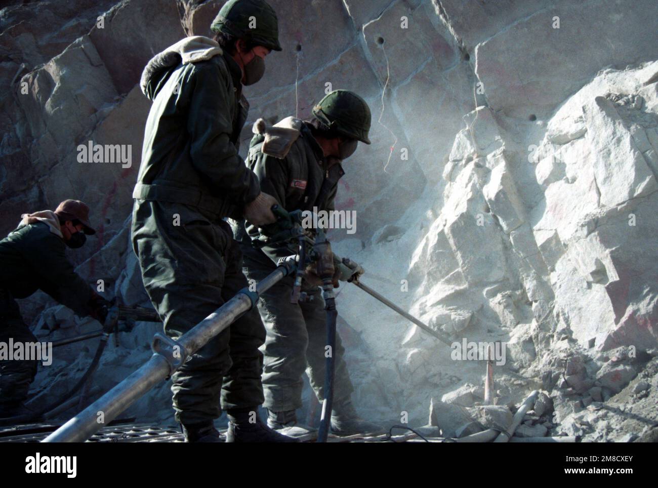 Workers bore holes for explosive charges in the rock face prior to the ...