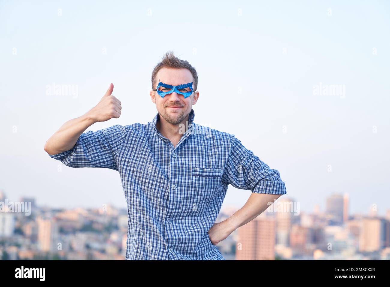 Cute caucasian man in nightwear shirt and superhero blue mask showing ...