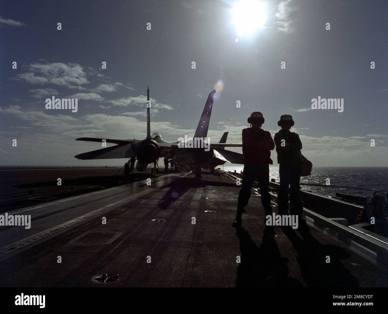 Two members of the flight deck crew stand near an F-14A Tomcat aircraft ...