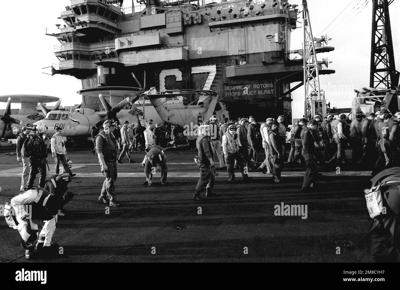 Dozens of crewmen walk slowly along the flight deck of the aircraft ...