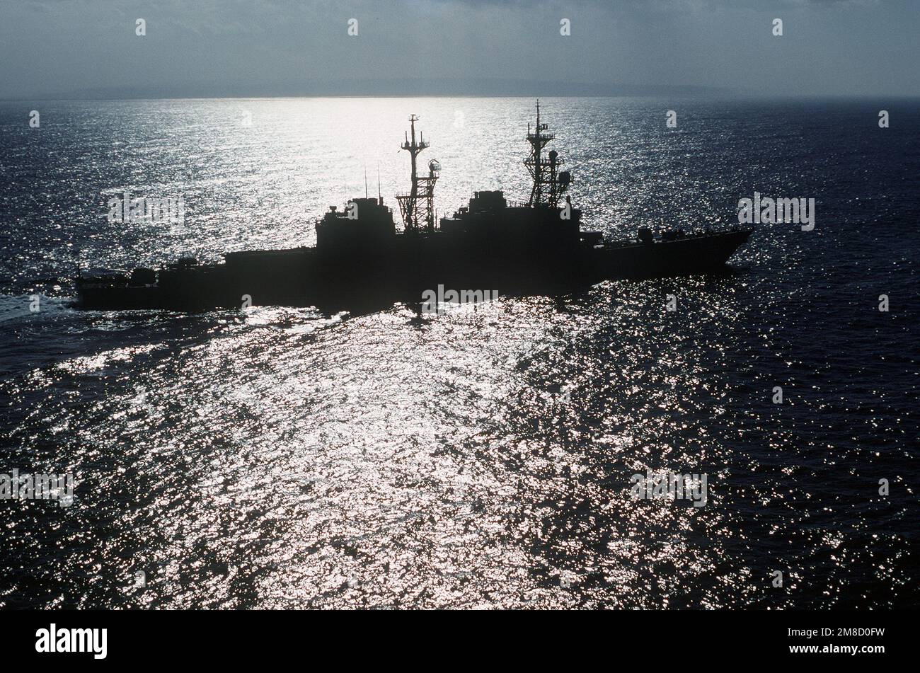 The destroyer USS CUSHING (DD-985) is silhouetted by the sun while ...