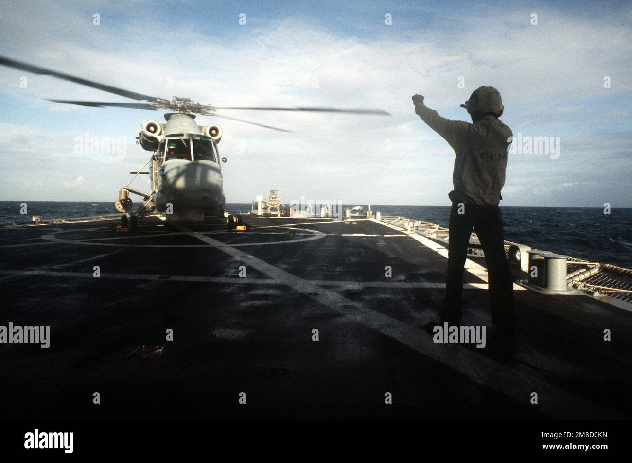 A squadron plane director signals to the pilot of an SH-2F Seasprite ...