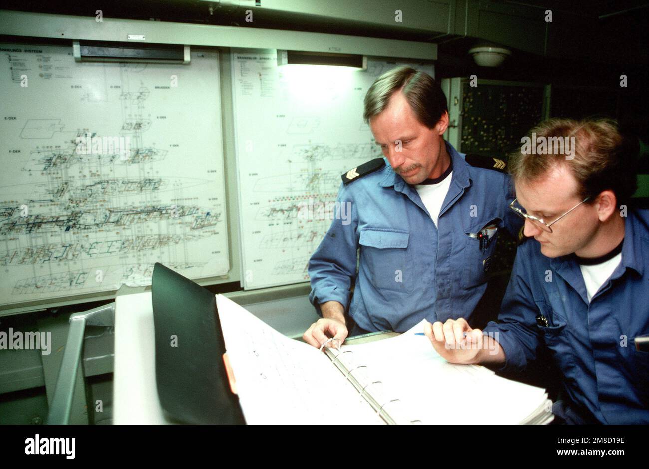 Two sailors look over a schematic diagram in the technical center ...