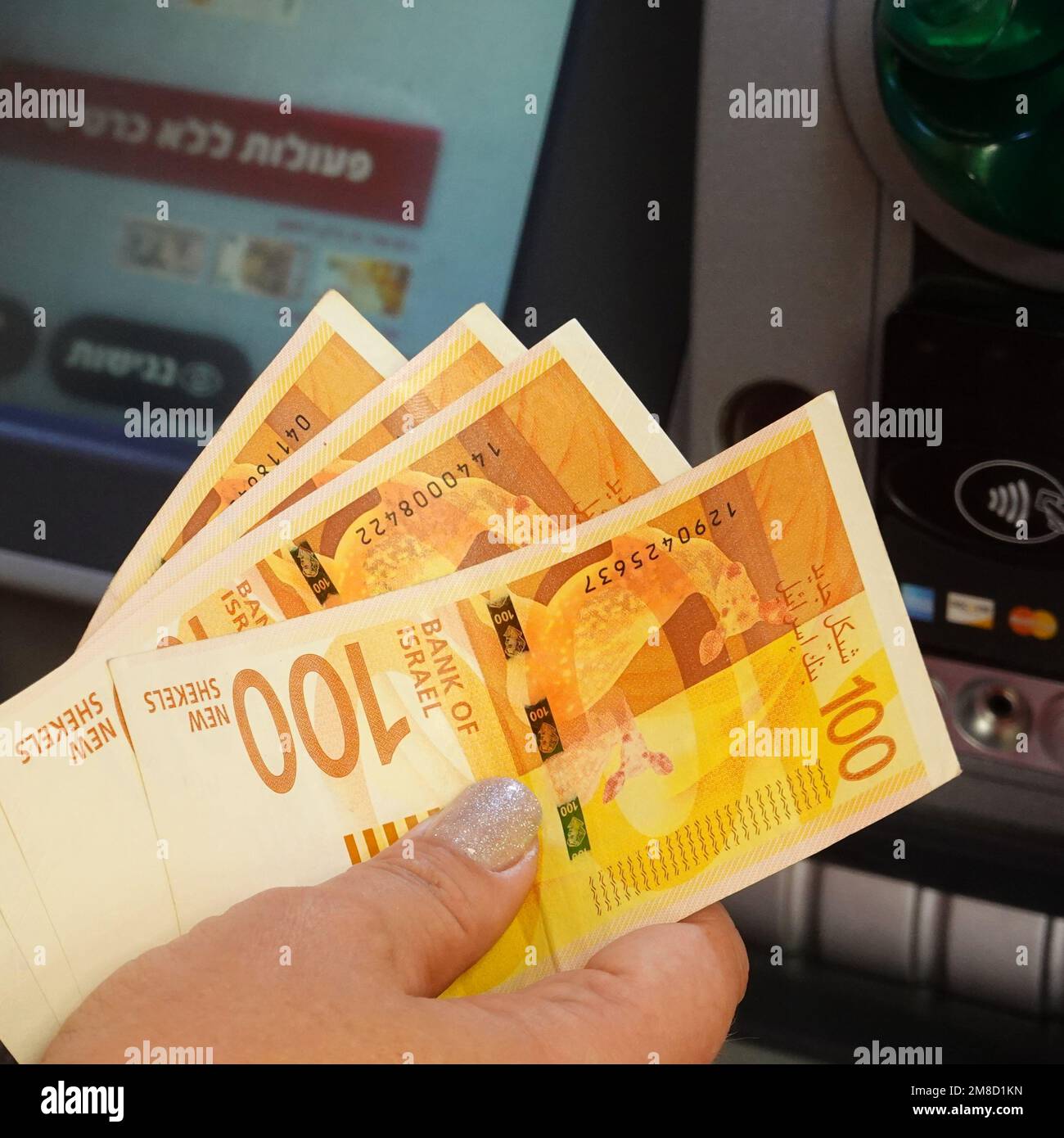 Woman’s hand holds banknotes of 100 new Israeli shekels behind the Cash ...