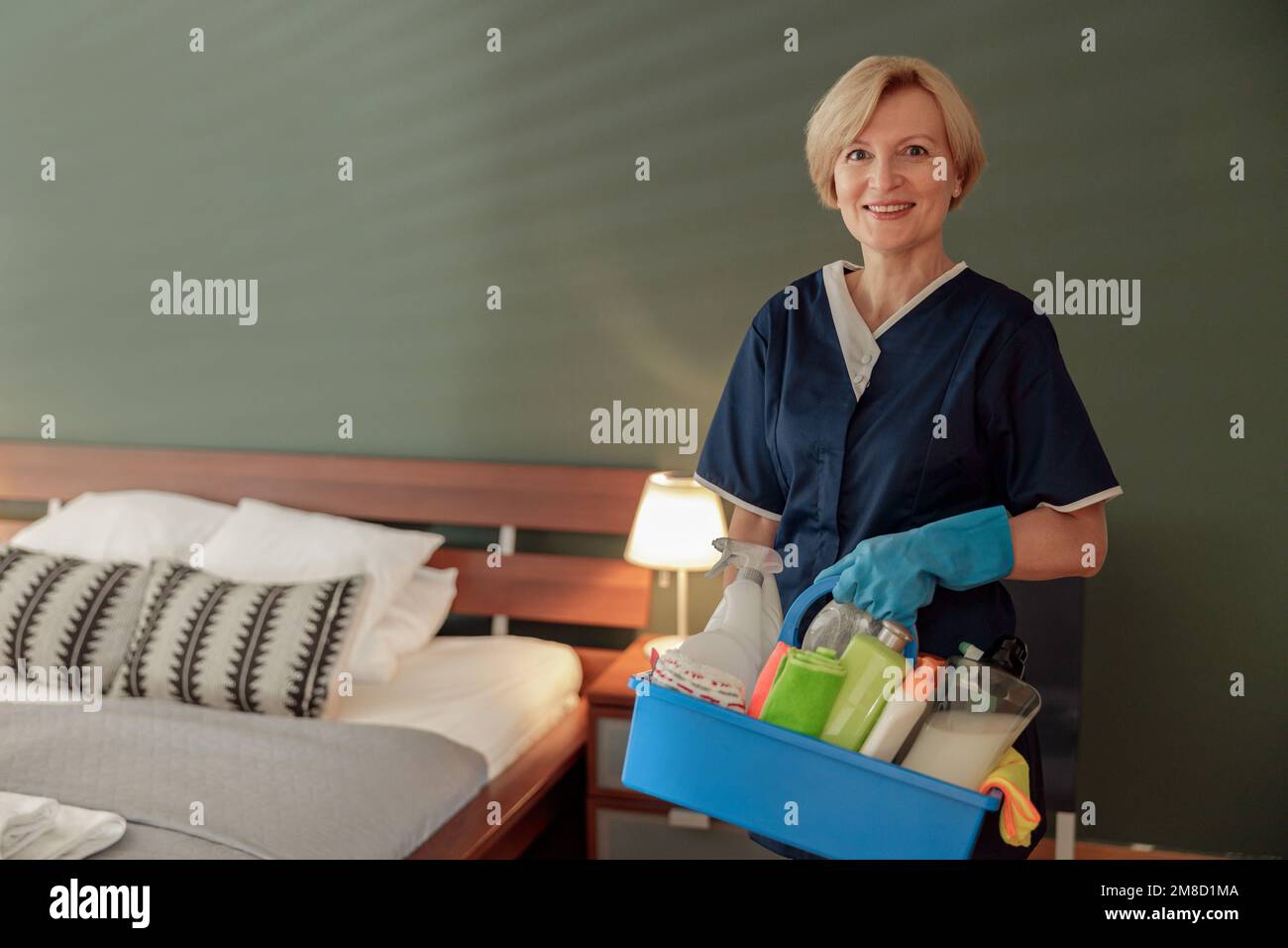 Housemaid in uniform for cleaning apartment holds box with detergents ...