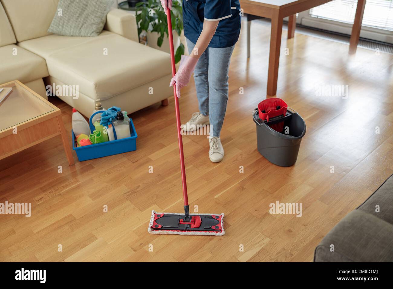 Unrecognizable woman washing floor with mop in living room ...