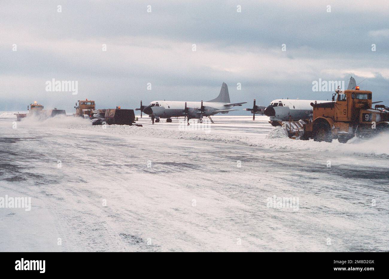 Heavy equipment removes snow from the flight line in front of a row of ...