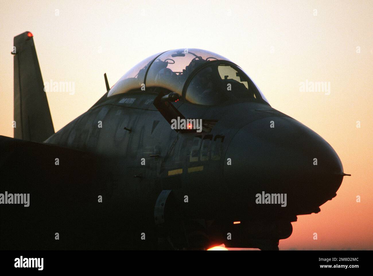 An F-14A Tomcat aircraft stands on a flight line at sunset. Country ...