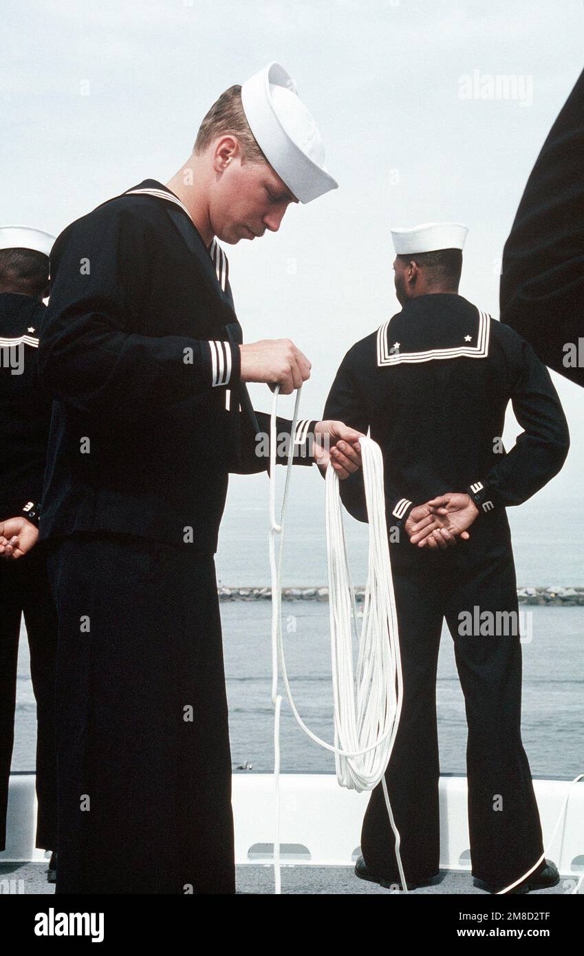 A sailor makes ready a messenger line that will be sent over the side ...