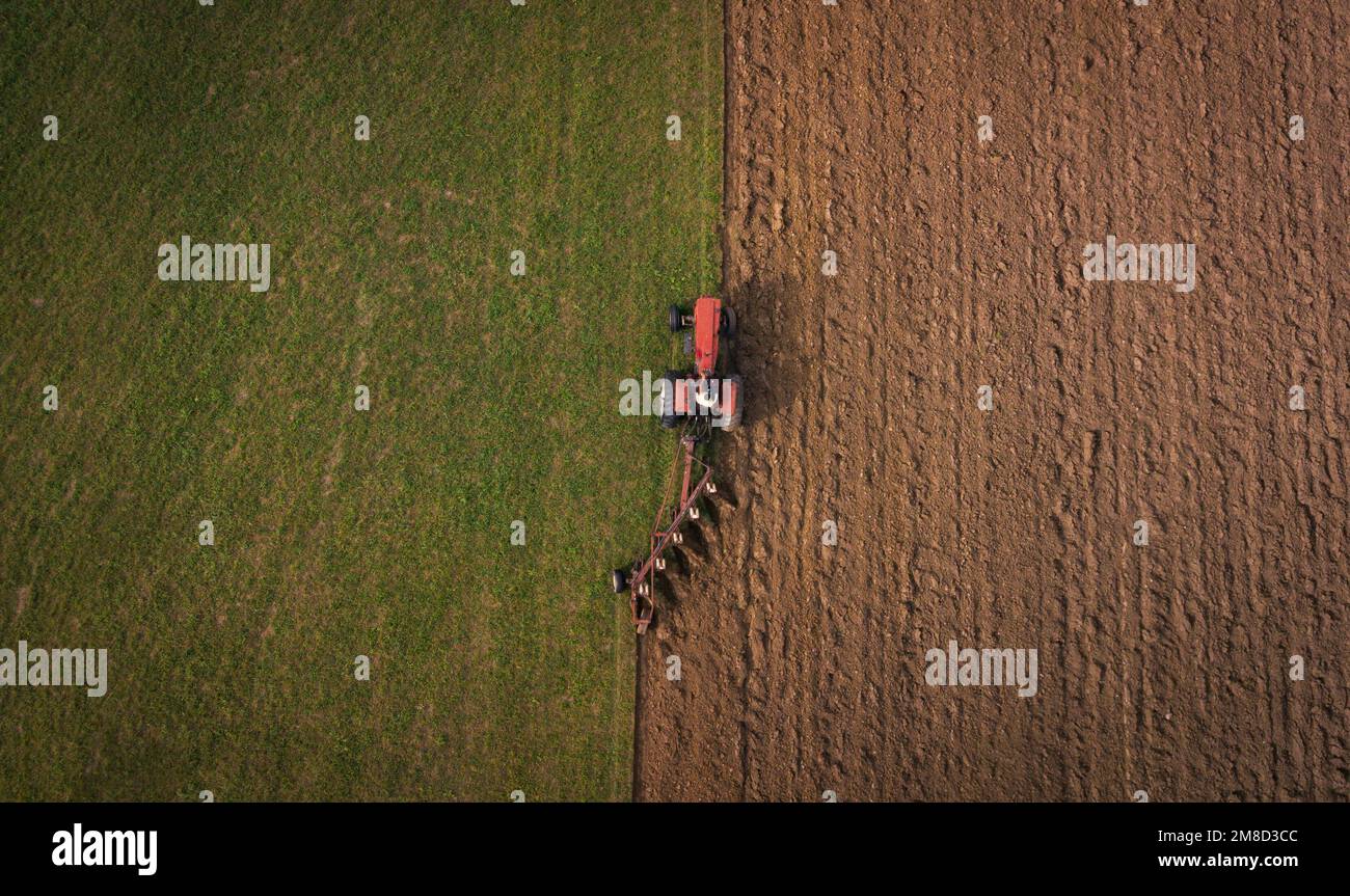 aerial shot of tractor plowing field in a countryside during early fall ...