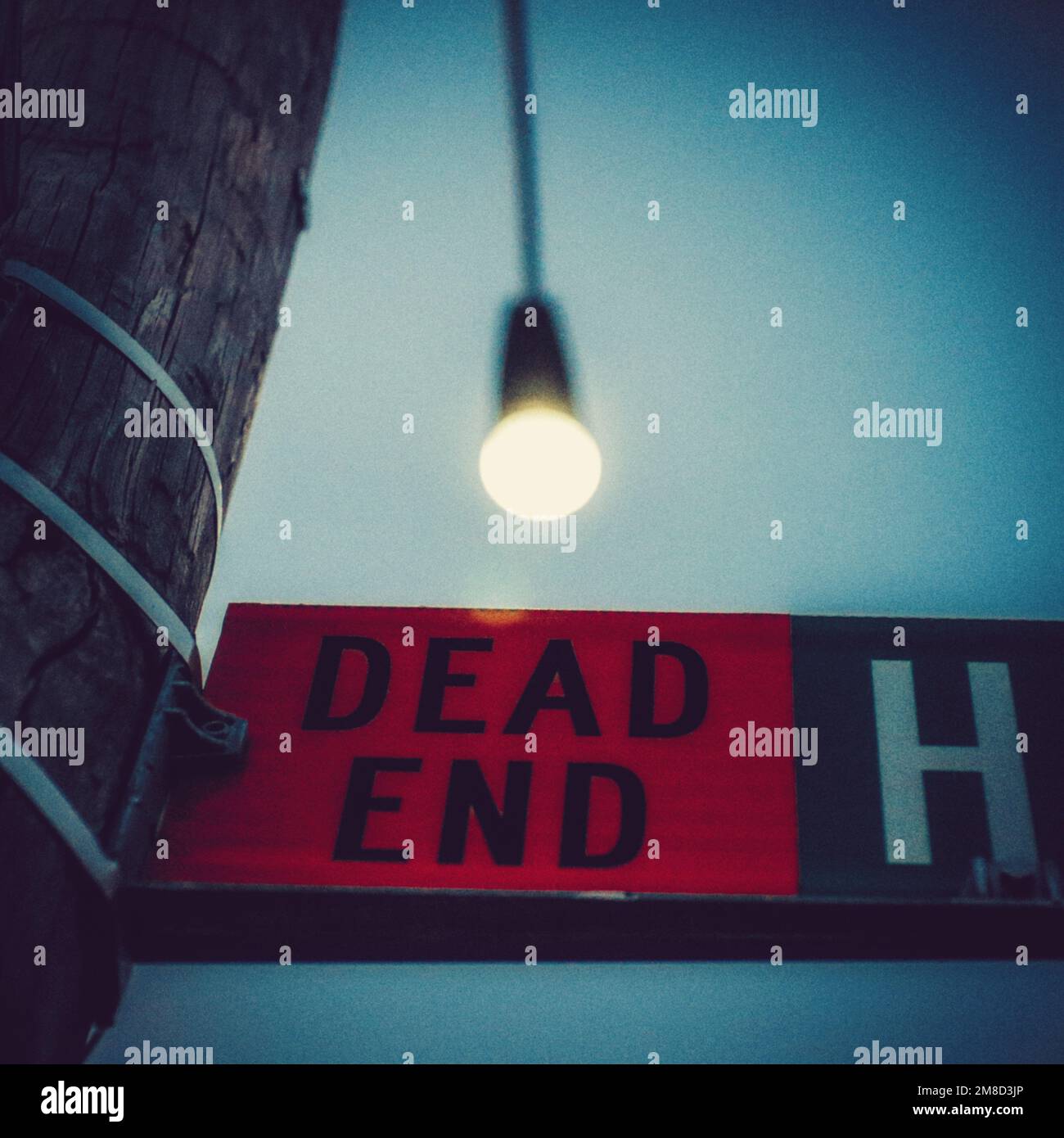 A Dead End sign with a blurred illuminated light bulb in the background ...