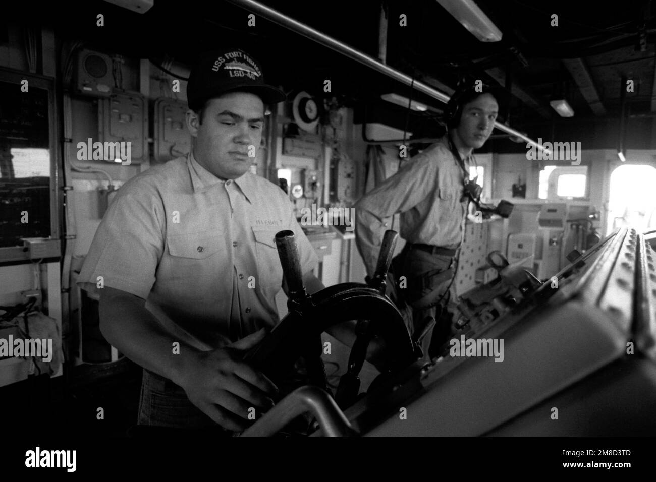 A sailor mans the helm on the bridge of the dock landing ship USS FORT ...