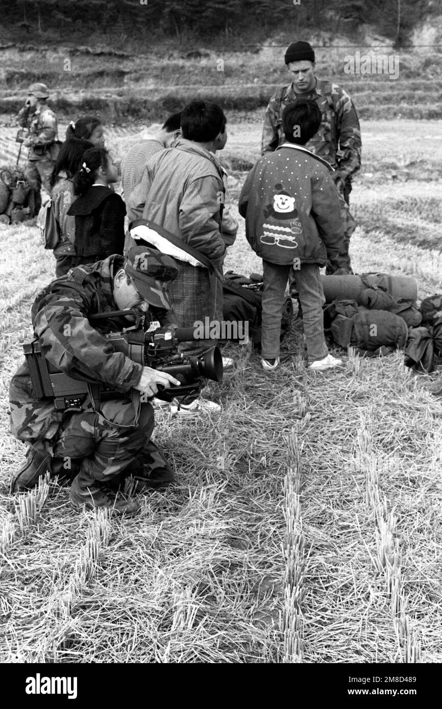 Korean children gather around a Marine as a Navy cameraman videotapes ...