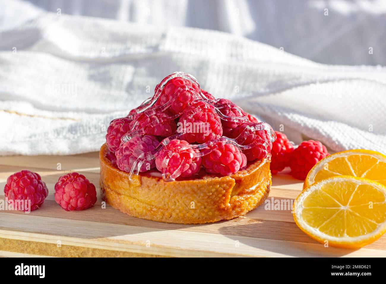 Pink fresh raspberry tart and fresh lemons on the kitchen table ...