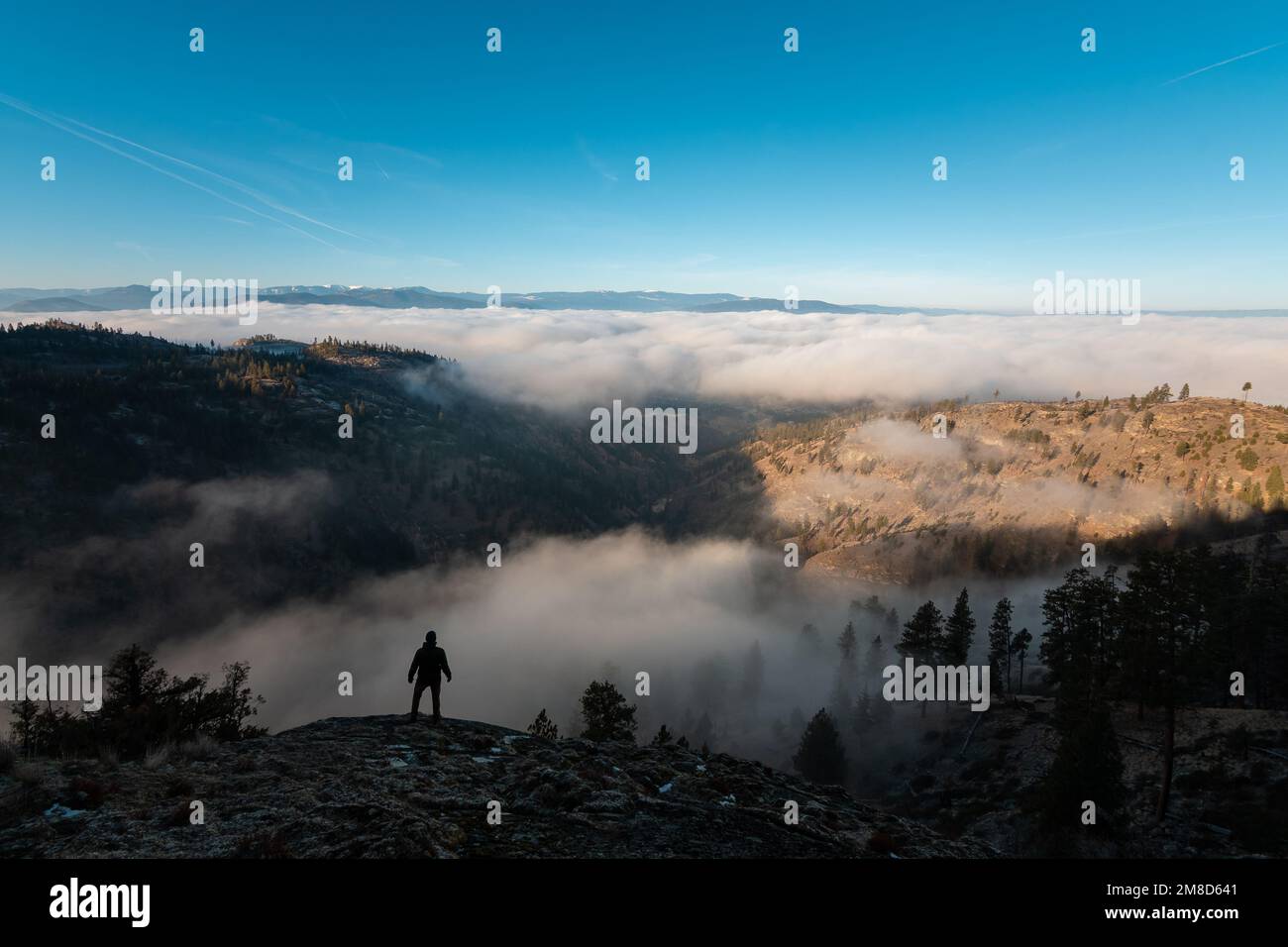 A high-angle view of mountains covered by clouds and a man standing on ...