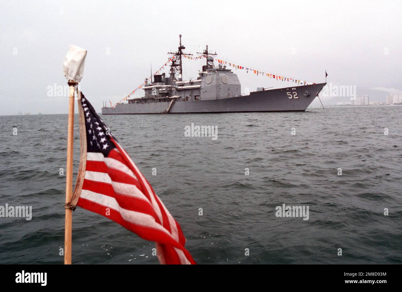 The American flag flies in the foreground as the guided missile cruiser ...