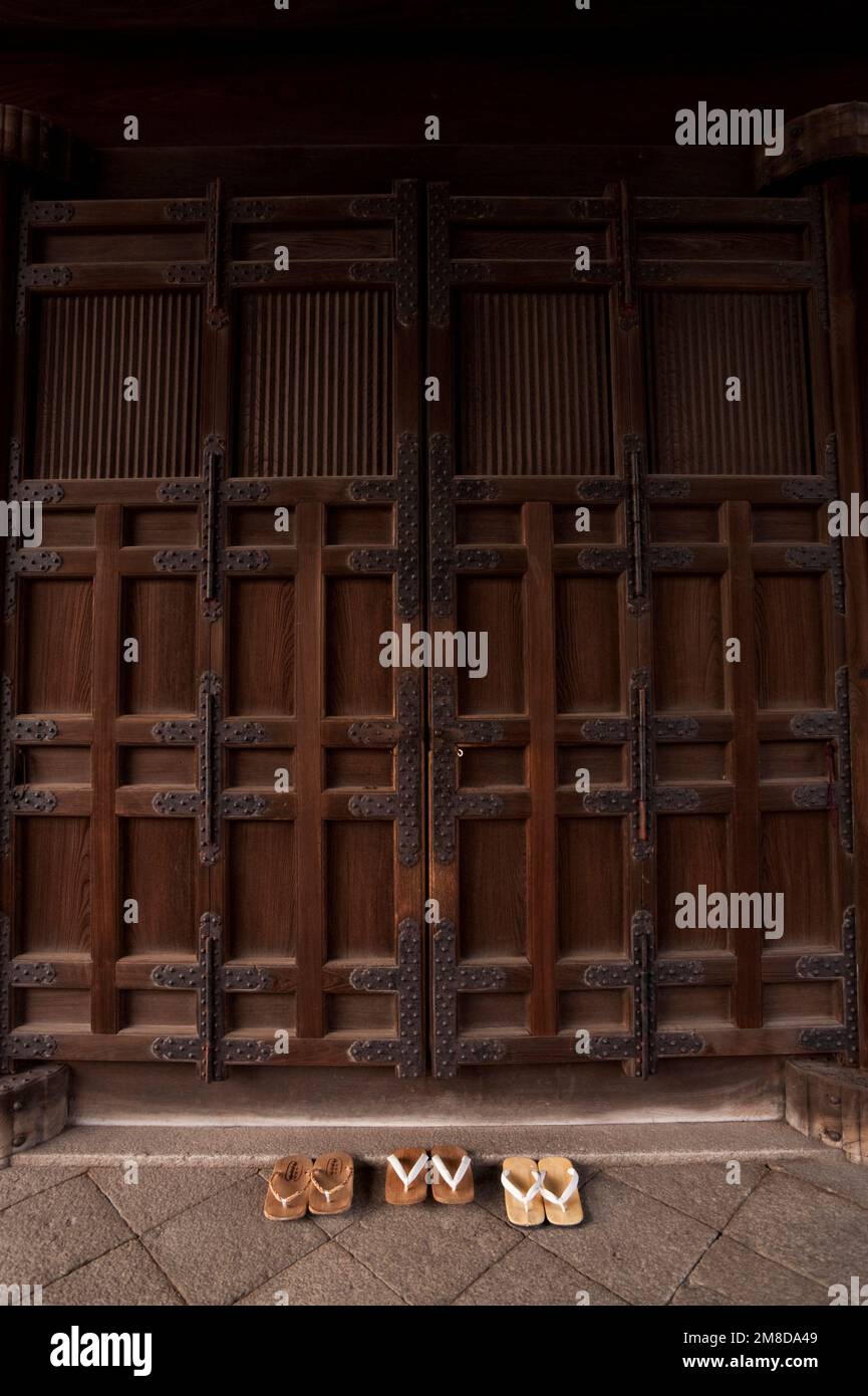 Traditional sandals are left outside the large wooden doors of a temple ...