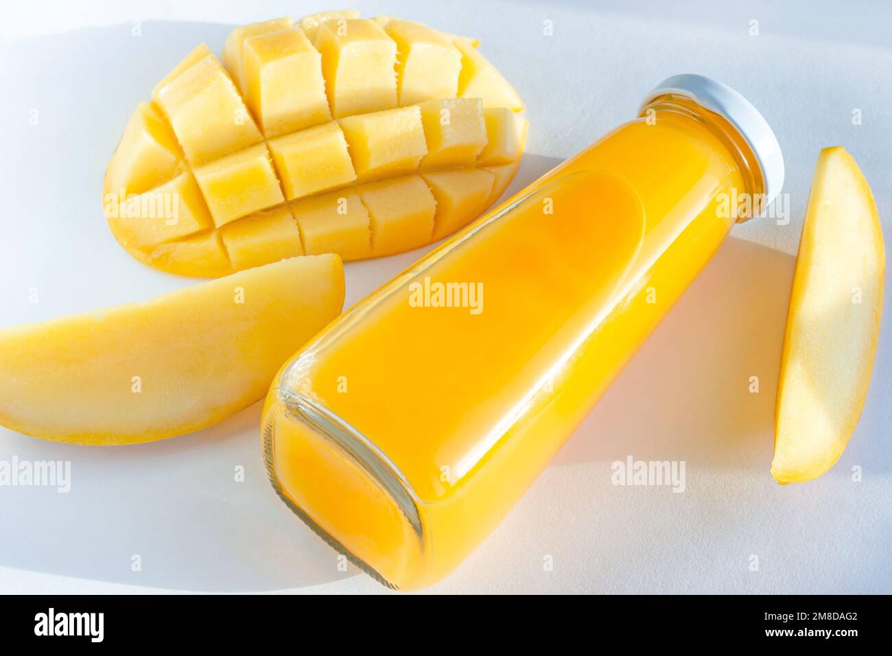 Bright yellow mango juice in a glass bottle with sliced fresh mangos on ...