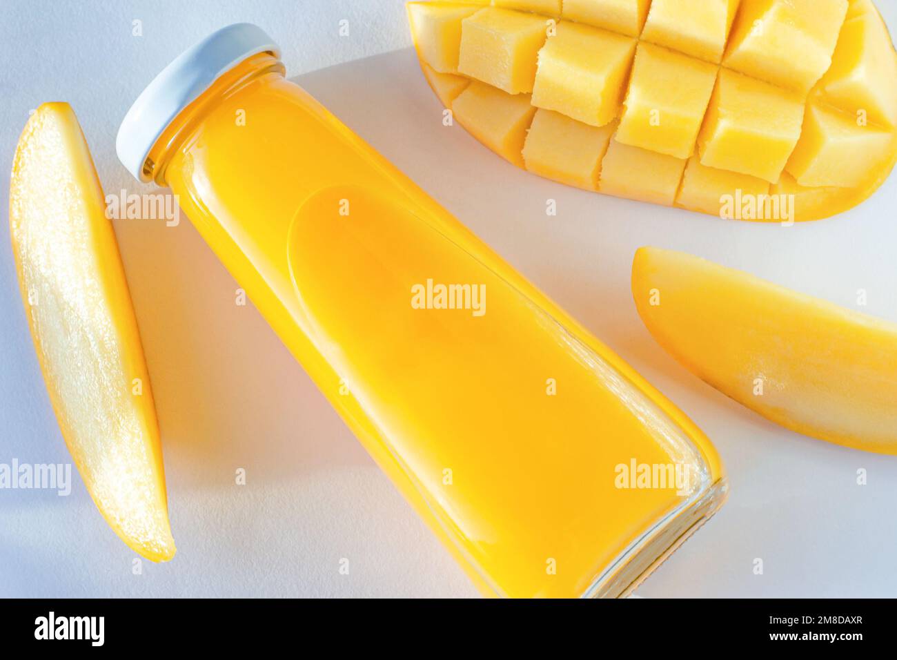 Bright yellow mango juice in a glass bottle with sliced fresh mangos on ...