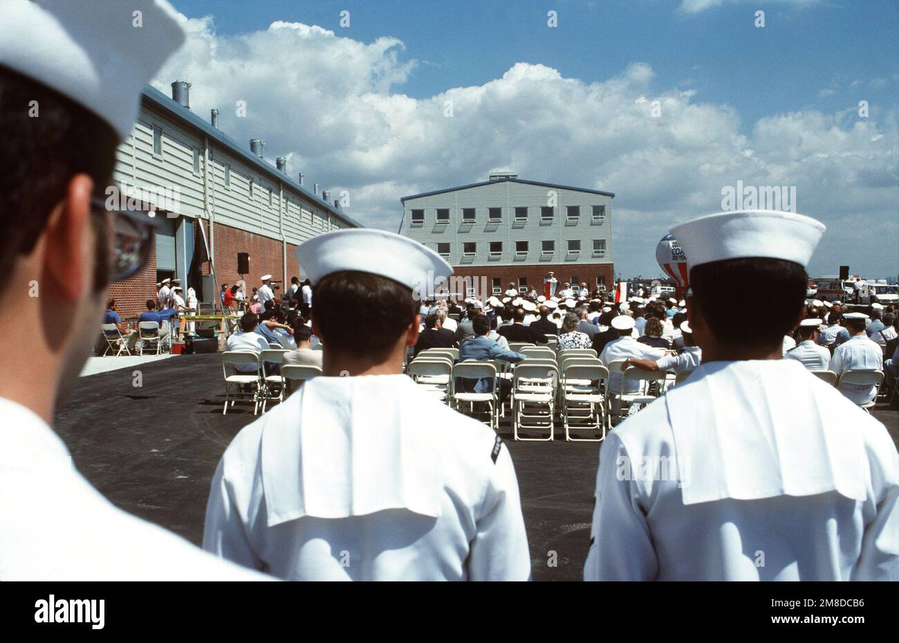 Sailors stand behind the crowd of officers and other guests listening ...