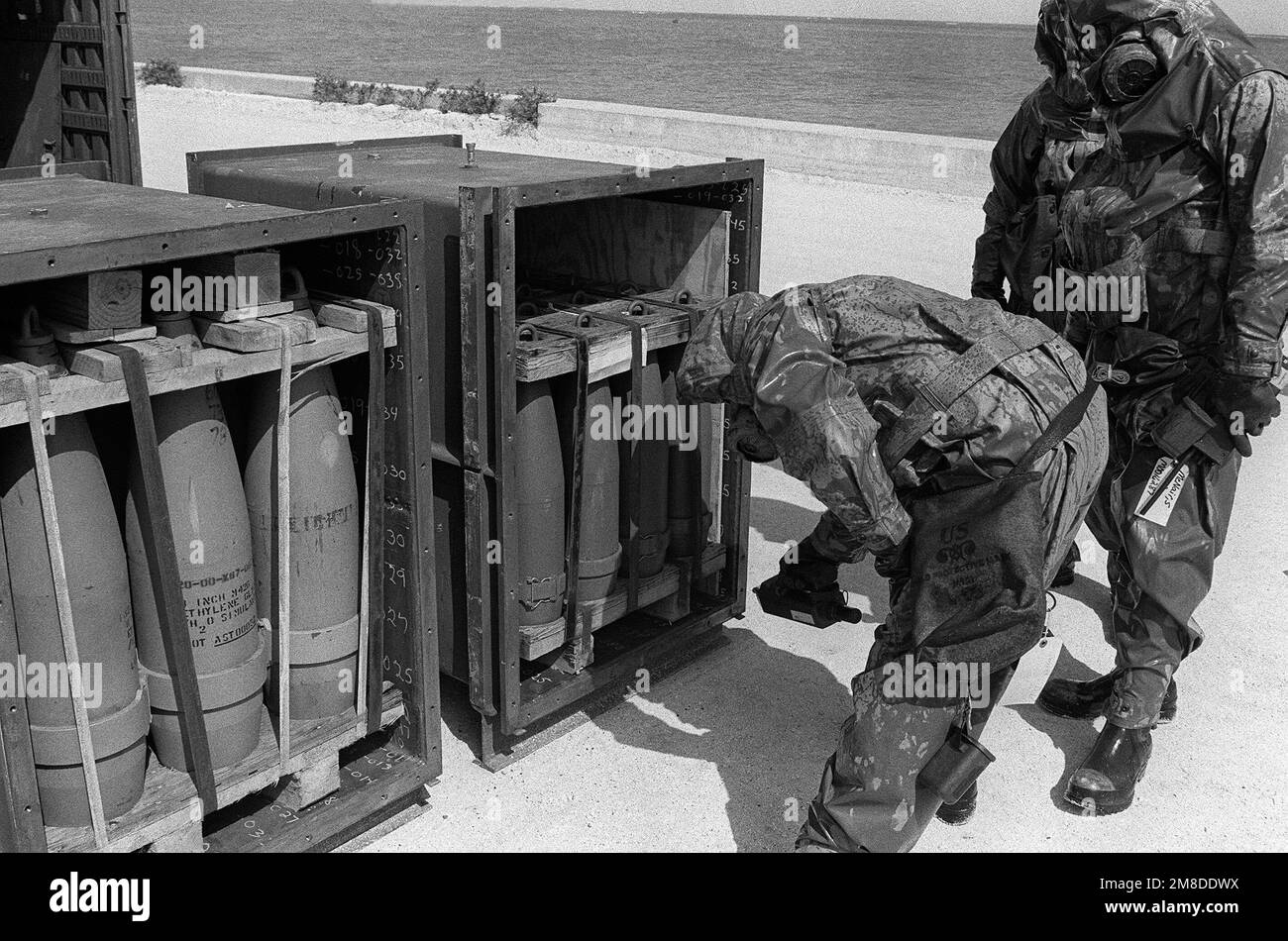 Two soldiers dressed in full protective gear look on as a third soldier ...