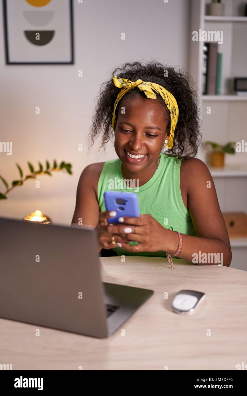 Vertical. Young African woman using phone at home office. Happy girl ...