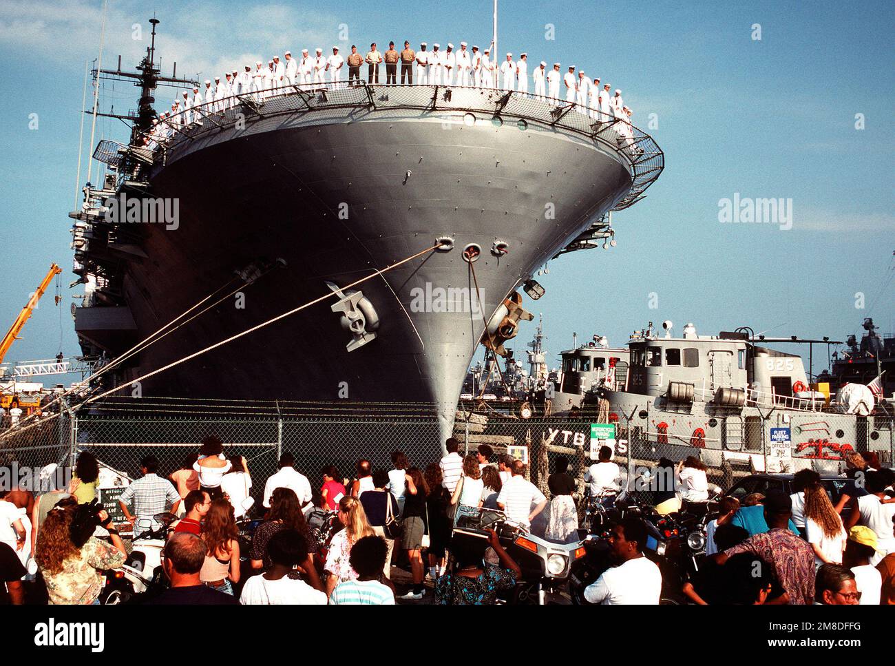 Family and friends watch from the pier as crew members man the rails ...
