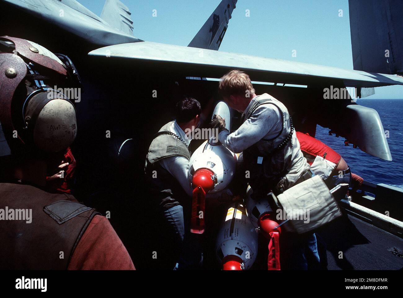 Flight deck crewmen help hoist a Mark 20 Rockeye II cluster bomb onto ...
