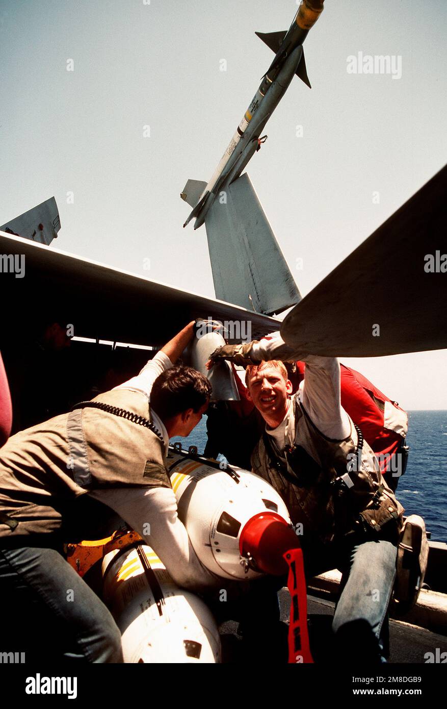 Flight deck crewmen help hoist a Mark 20 Rockeye II cluster bomb onto ...