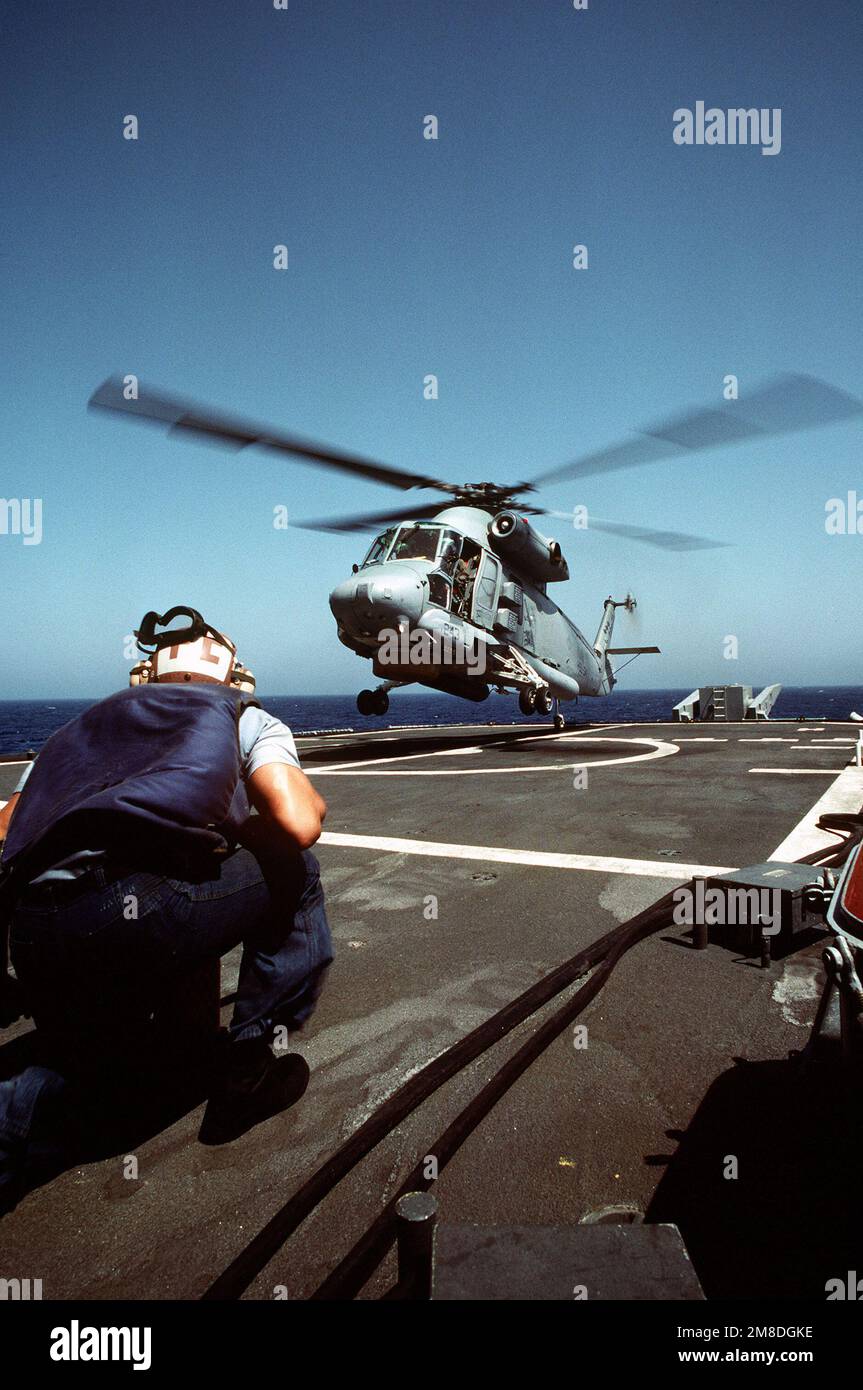 A sailor stands by with wheel chocks and tie-down chains as an SH-2F ...
