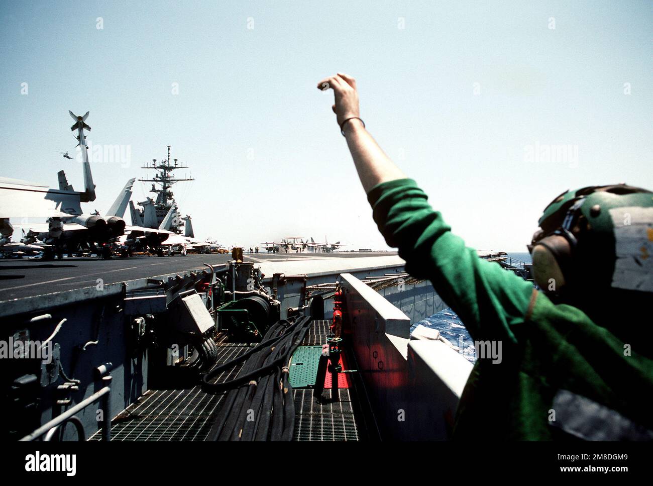 A squadron maintenance crewman signals from a catwalk aboard the ...