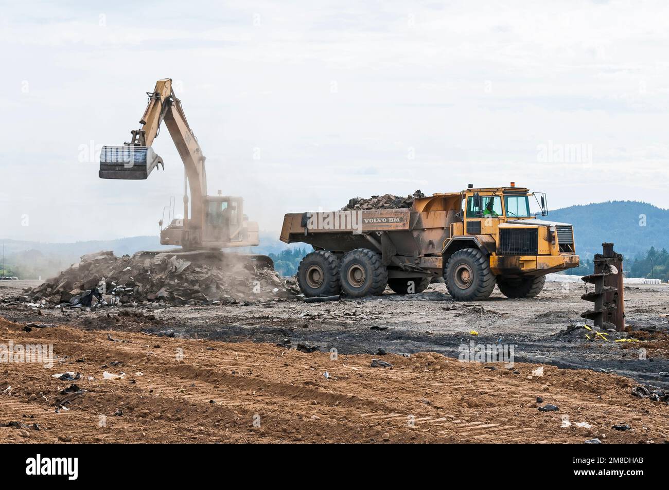 A power shovel loads debris onto a dump truck in an active landfill ...