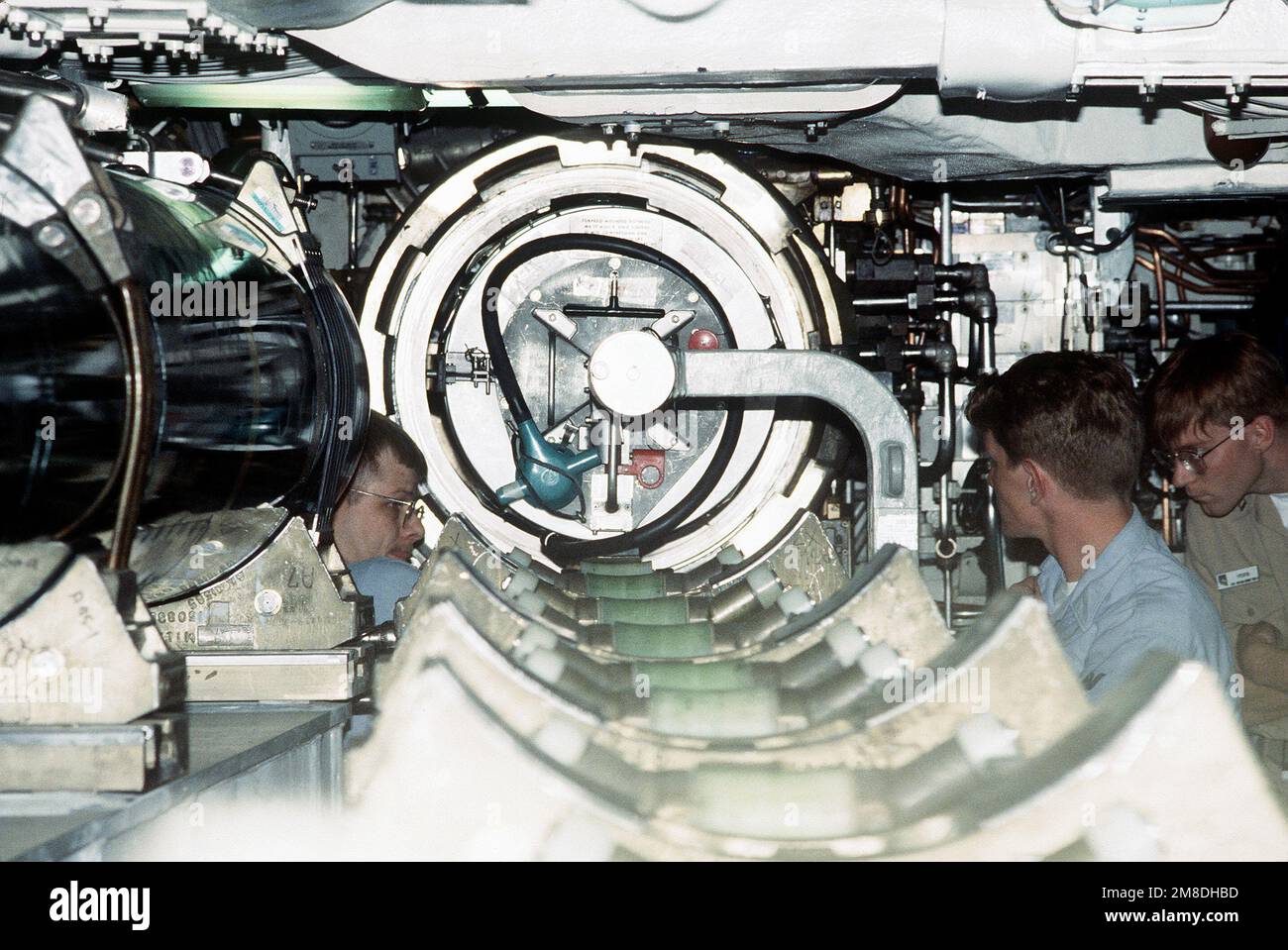 Crew members examine the aft end of a torpedo tube in the torpedo room ...