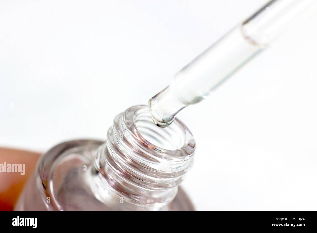 The pipette dropping a transparent liquid into dropper bottle on light ...