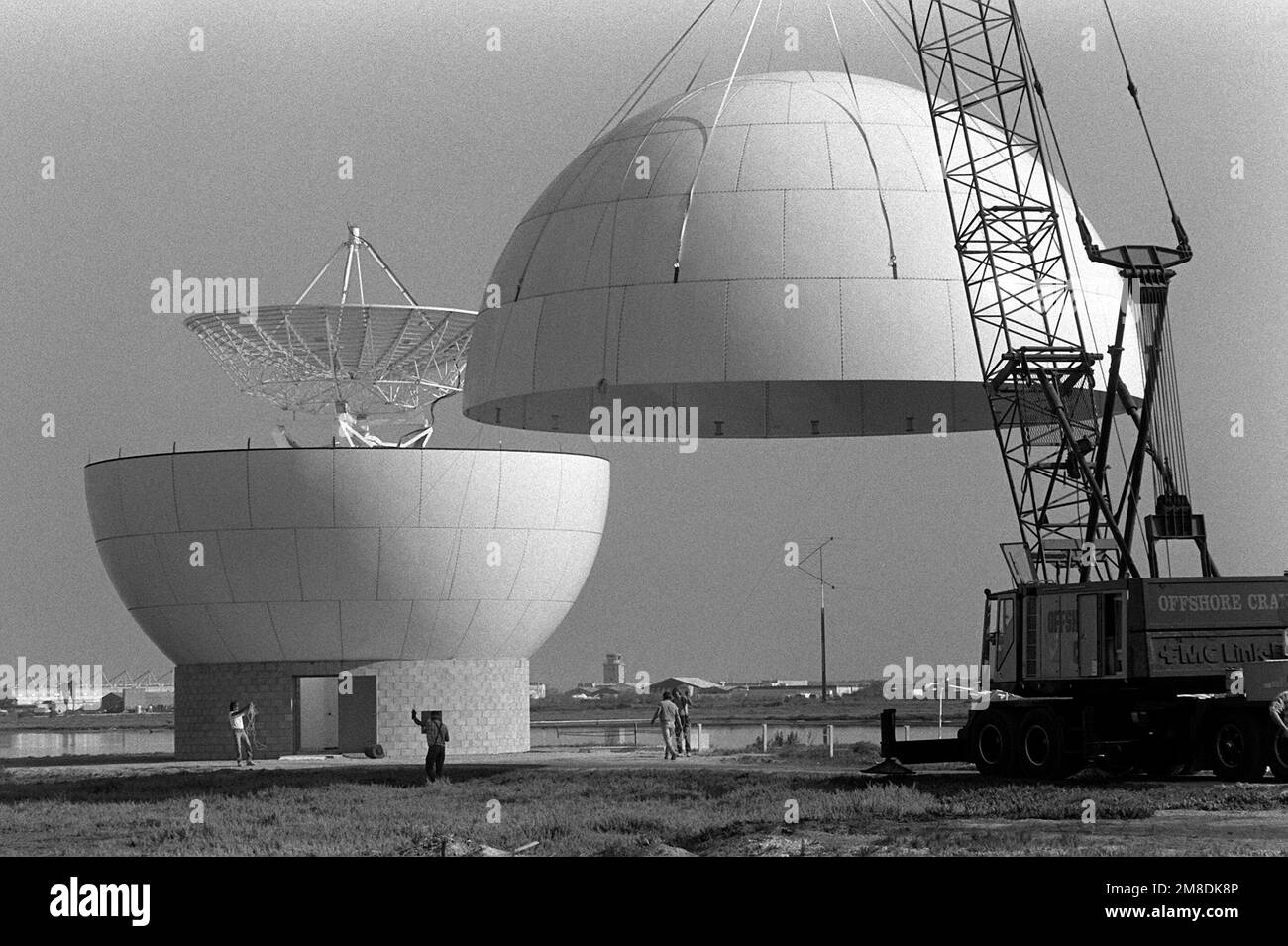 Workers hold onto guide cables as the upper half of a radome enclosure ...