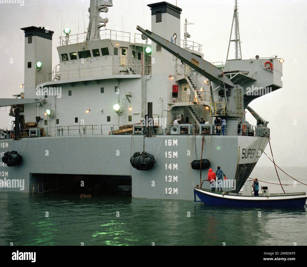 Crewmen in a small boat come alongside the partially submerged ...