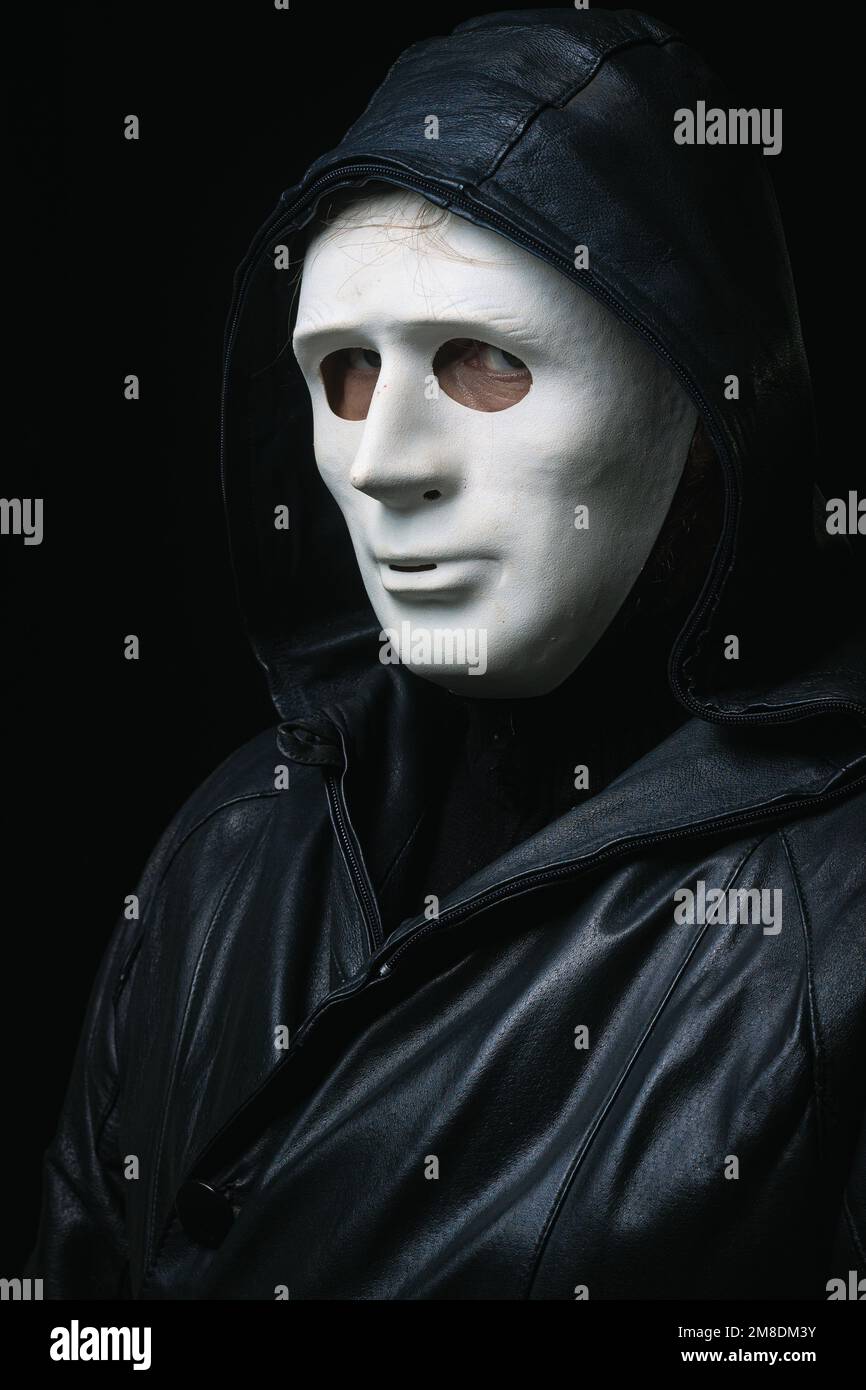 Man in terrible face mask staring at camera against dark background ...