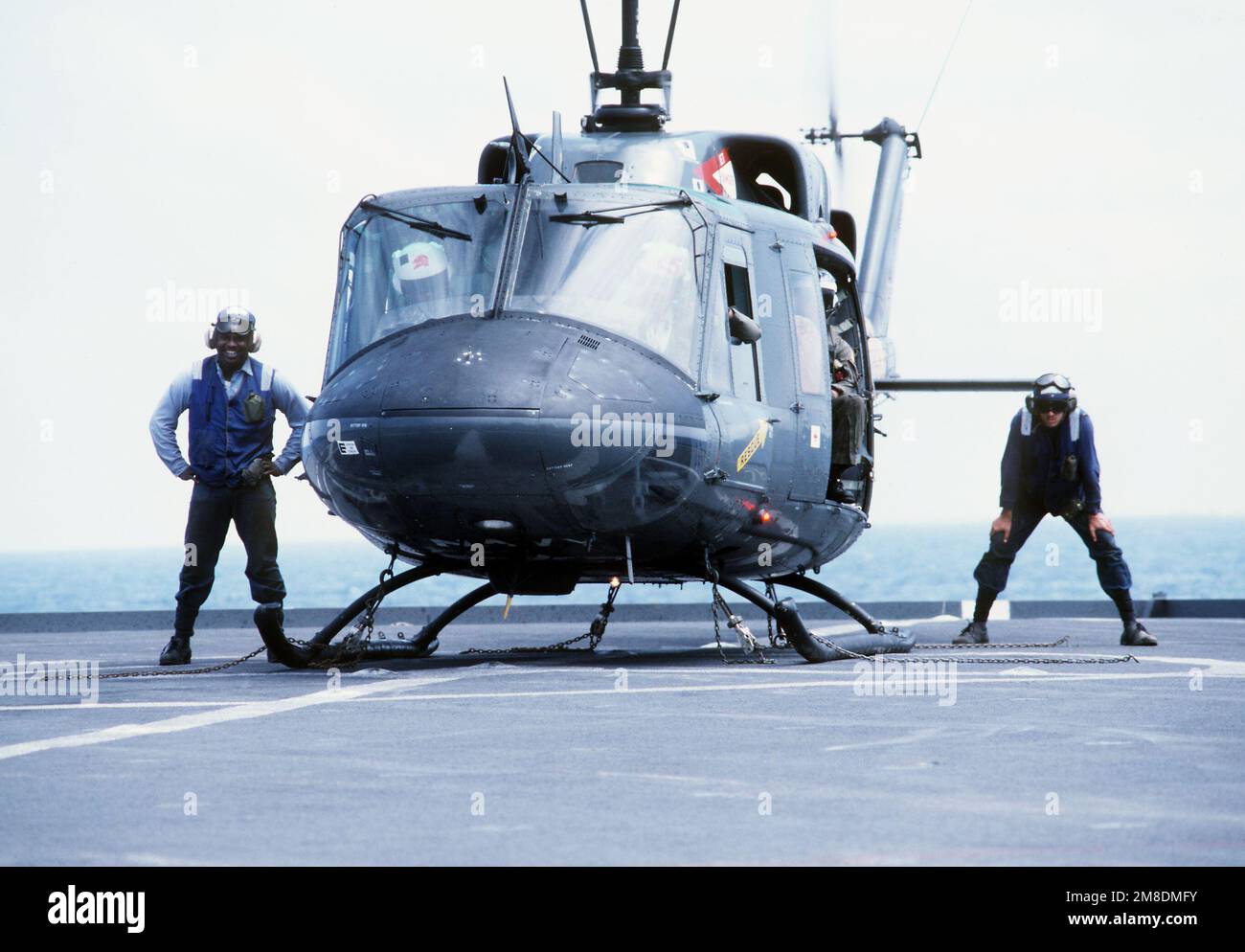 Two flight deck crewmen stand by to remove the tie-down chains from a ...