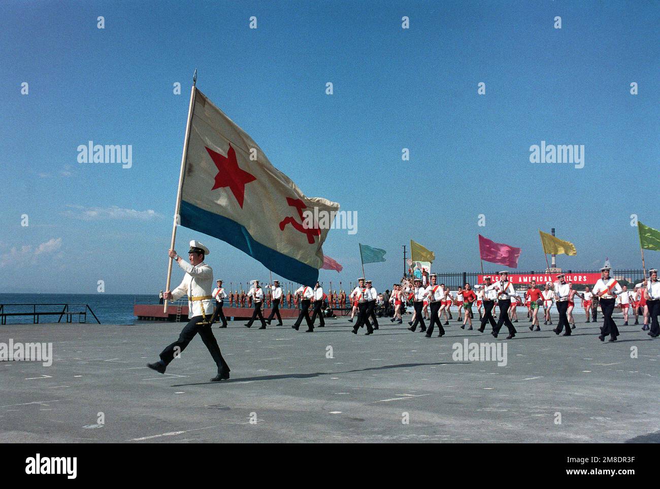 An officer carries the Soviet naval ensign as he leads a review of ...