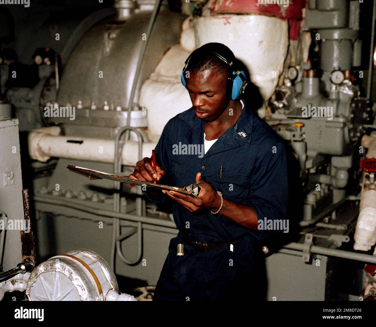 A crew member writes notations in an engineering space aboard the ...